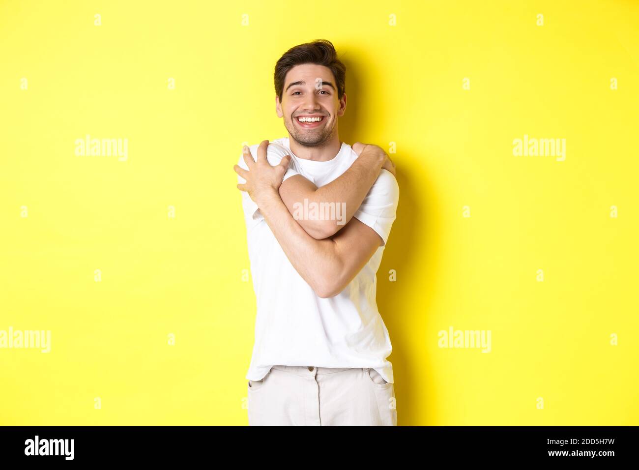 Happy kind guy hugging himself and smiling, standing pleased against ...