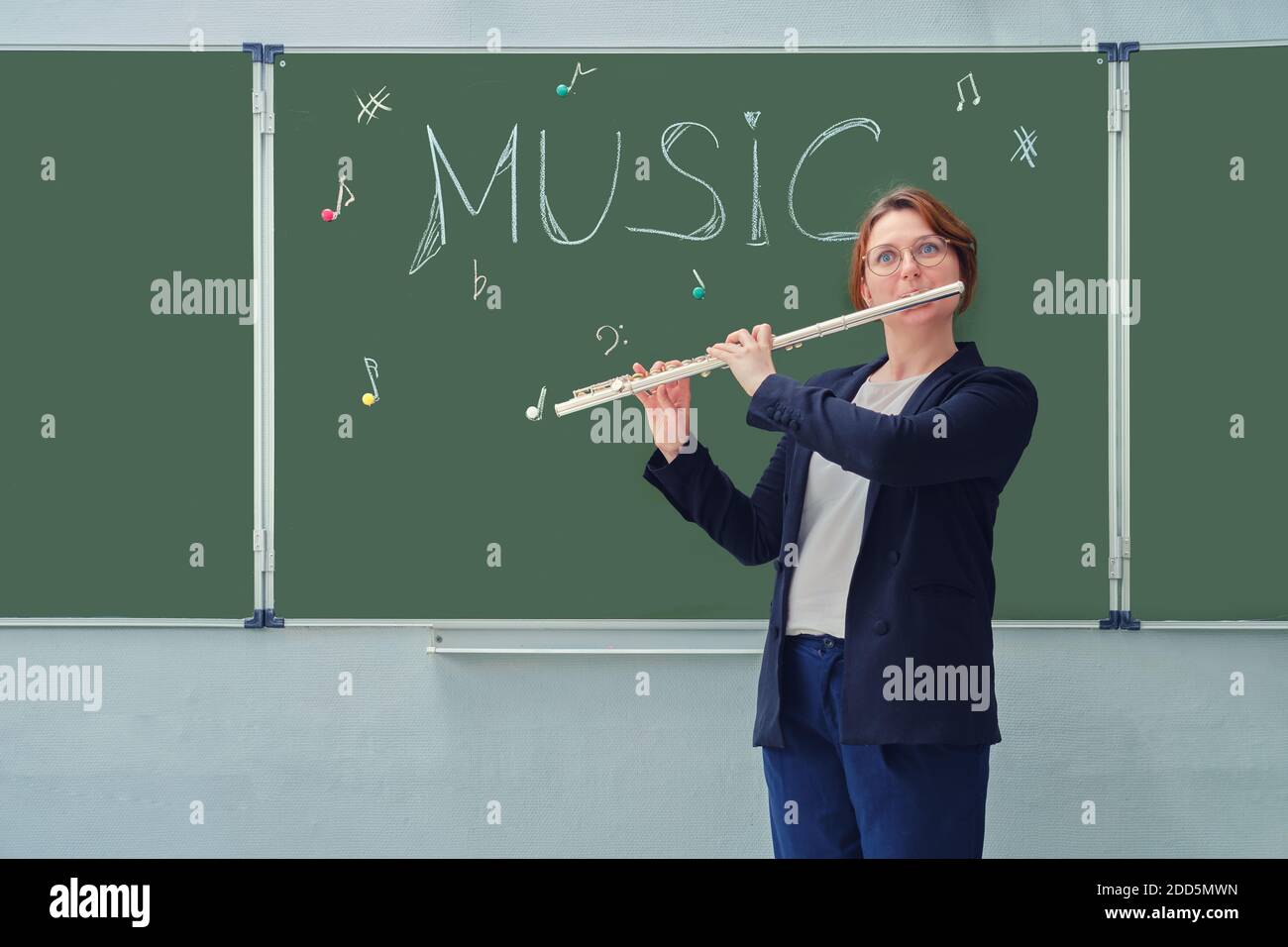 A music teacher with a flute stands next to a blackboard in a school ...