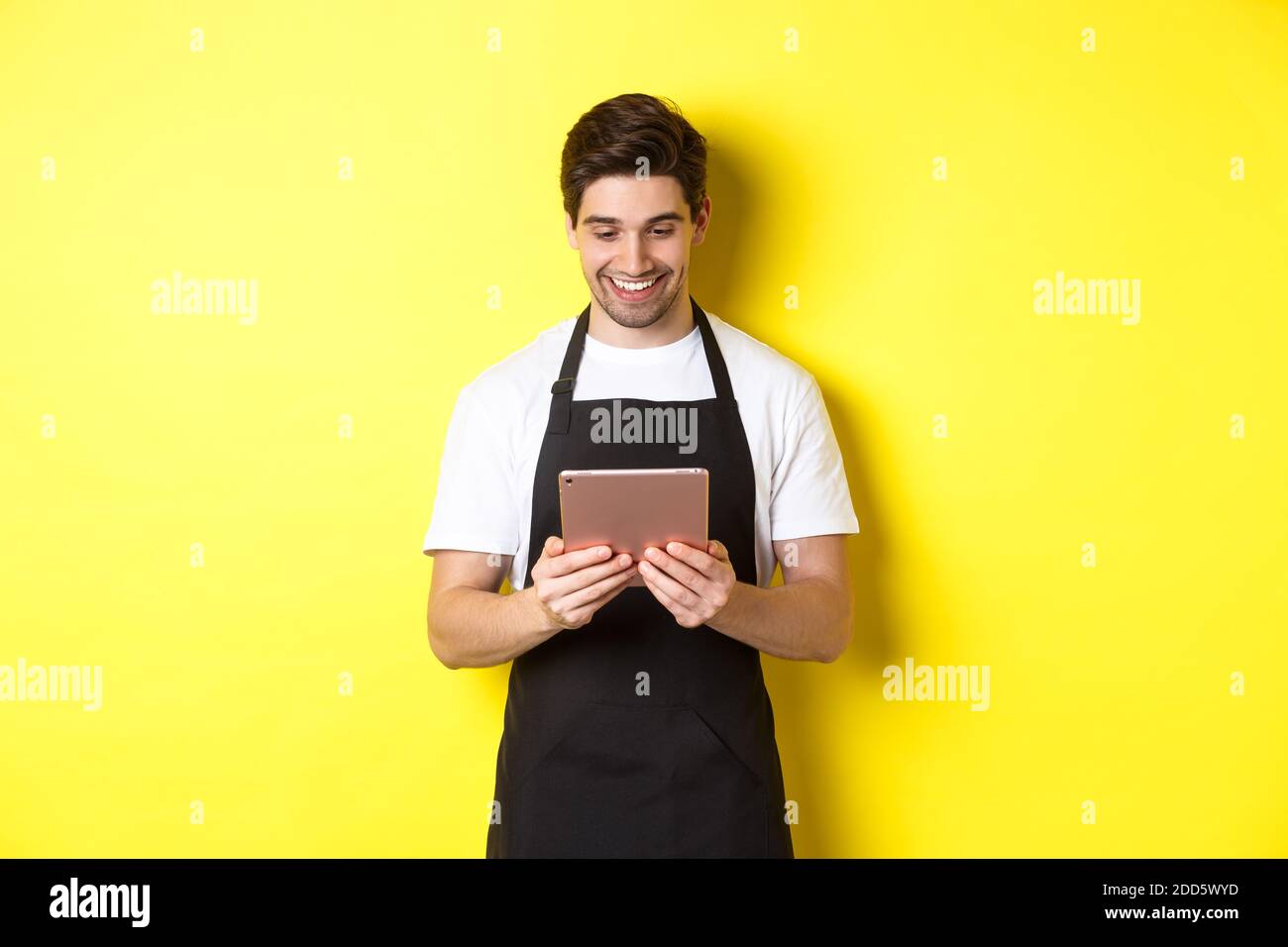 Seller in black apron looking at digital tablet screen, smiling pleased ...
