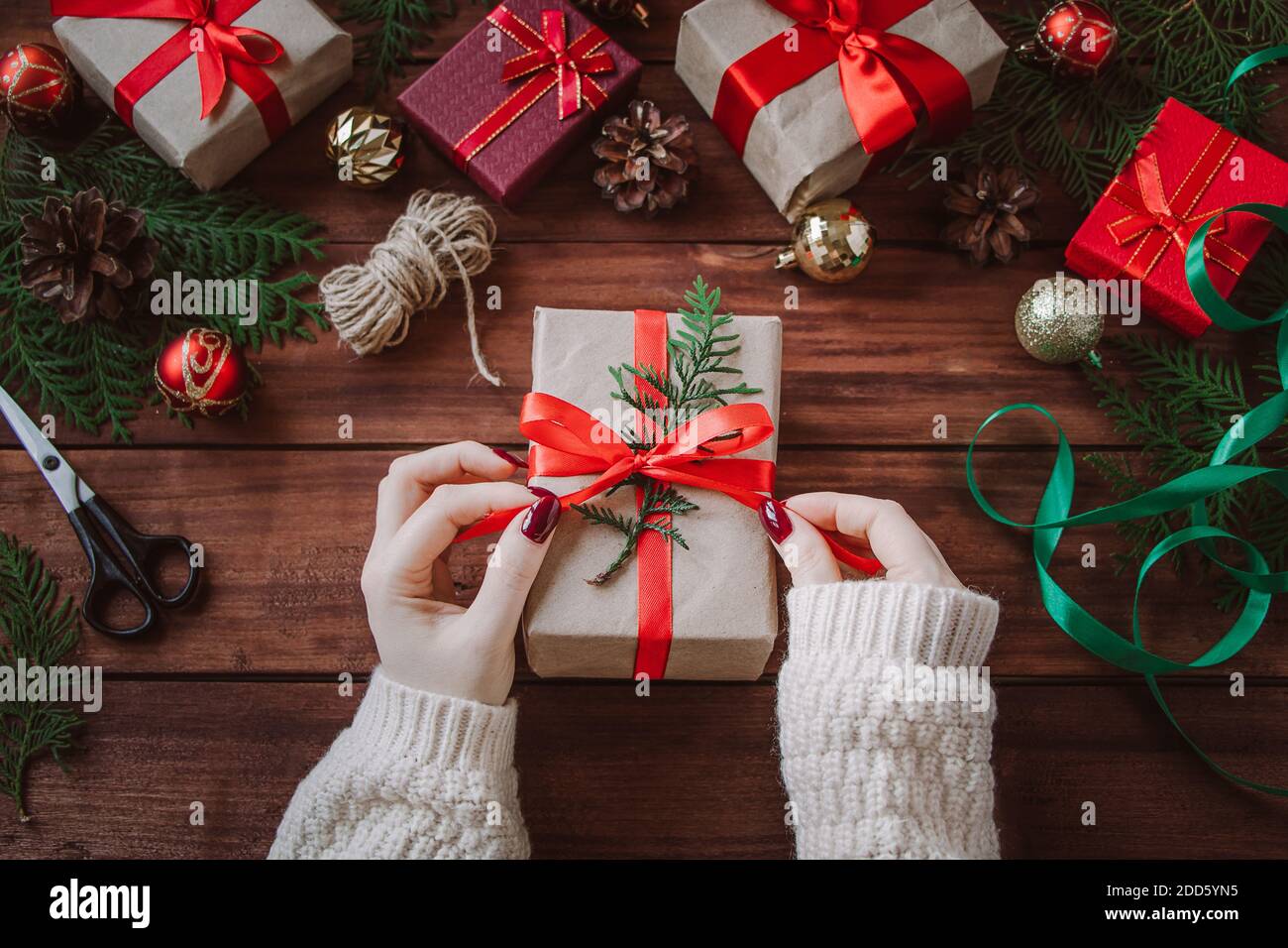 Christmas gift wrapping process. Woman decorates box with a red ribbon ...