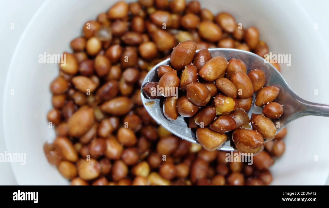 A spoonful of fried peanuts, coated with skin. With a bowl of peanuts ...