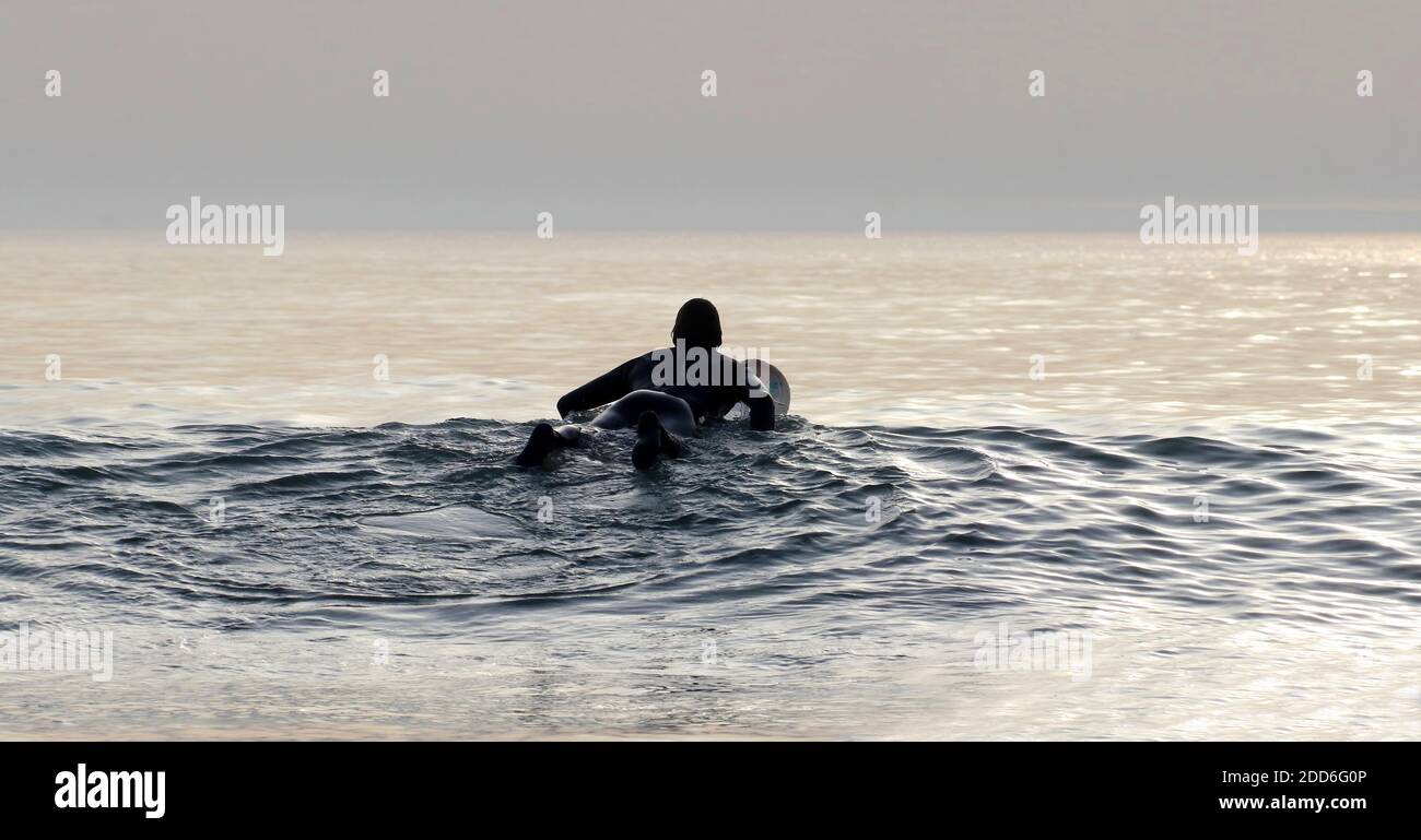 single male surfer laying on his board waiting for the right wave Stock ...