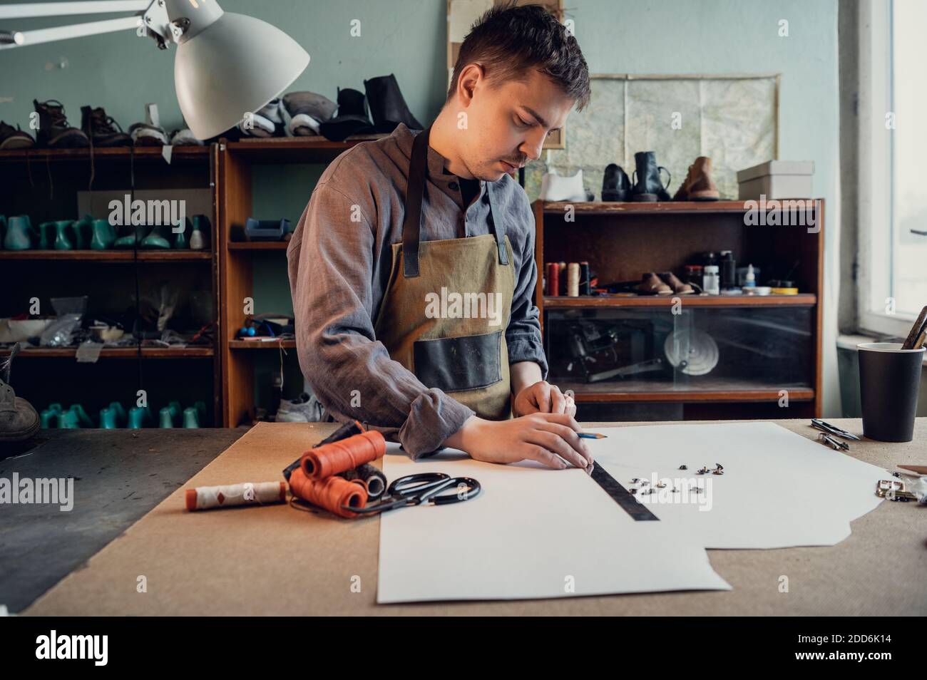 A young shoemaker makes a drawing for a pattern for leather shoes on a ...