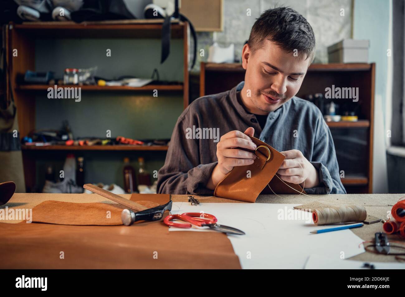A young shoemaker manually sews decorative elements to leather shoes in ...