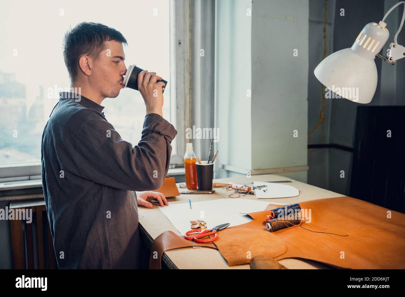 A young shoemaker guy has taken a break from work and is drinking from ...