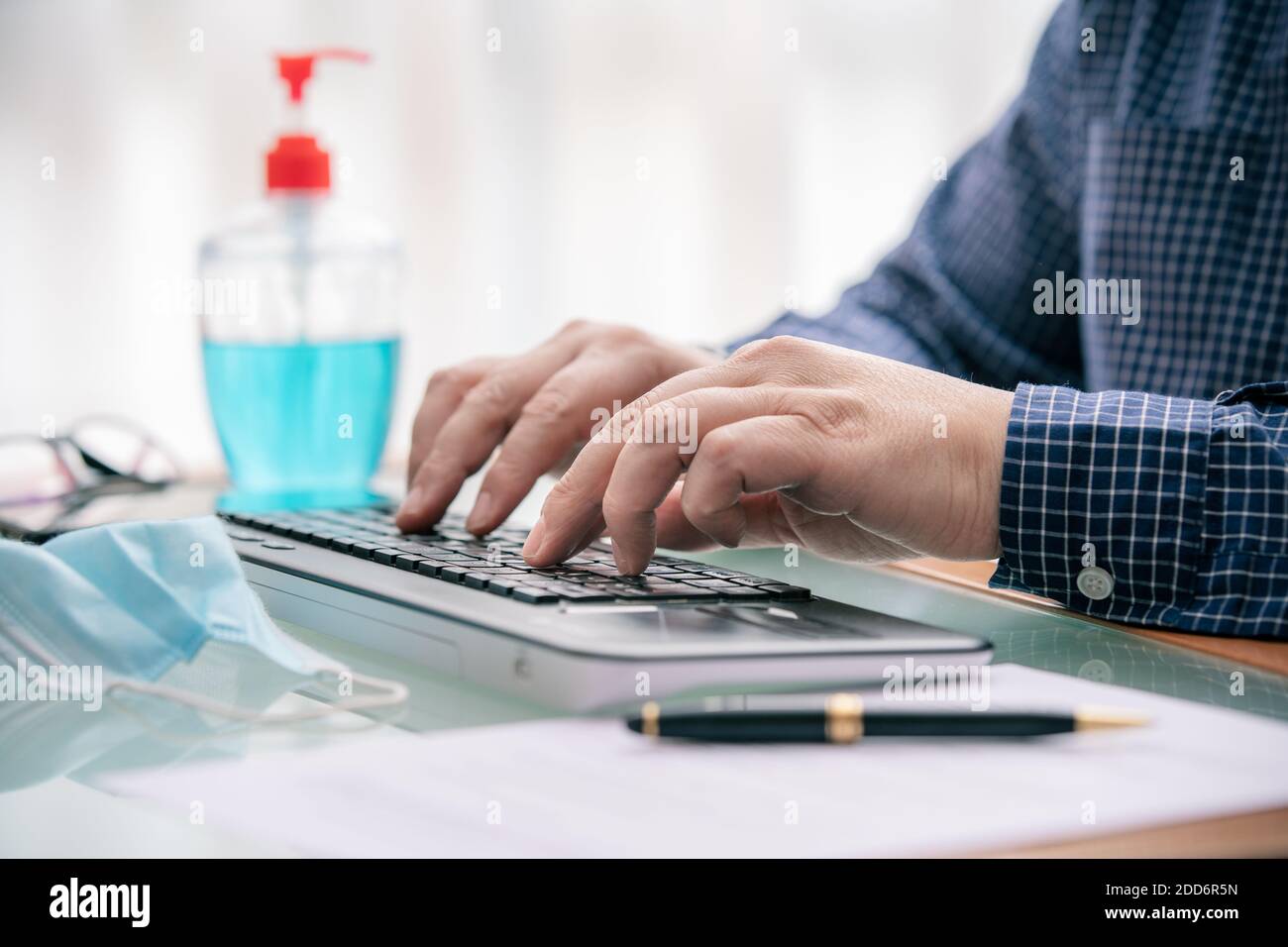 Hands typing computer while teleworking with mask and hydrogel on the ...