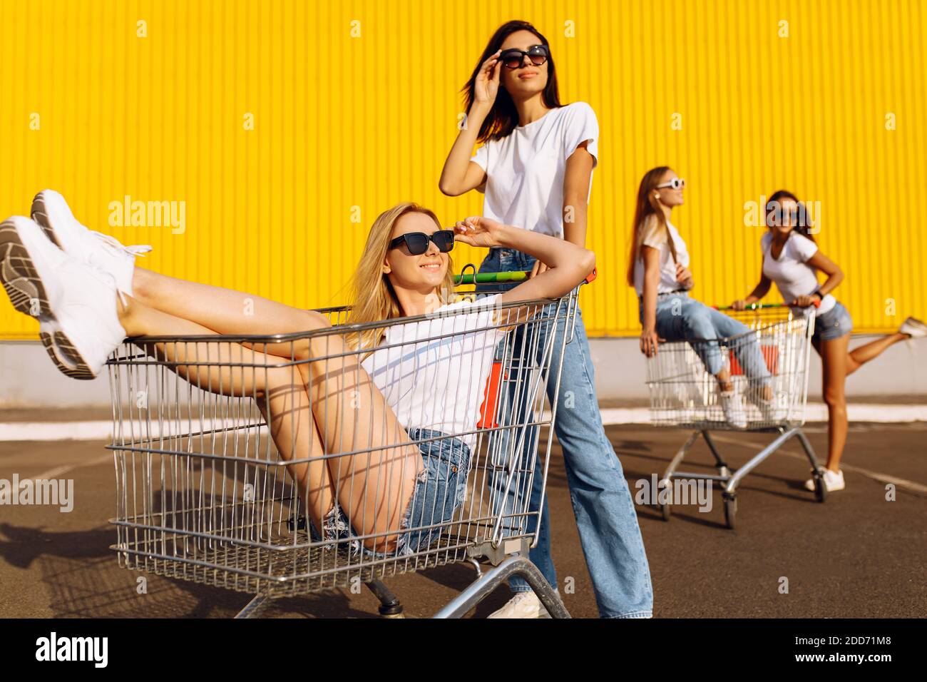young smiling women friends having fun with shopping cart in city near ...