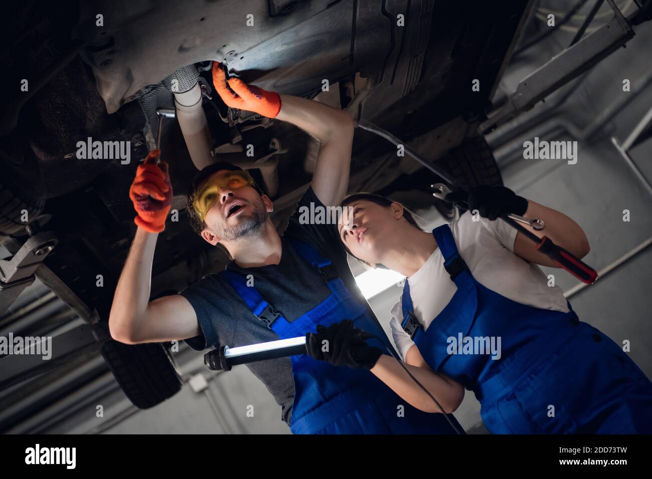 A female worker is holding a flashlight. Repairer fixing a lifted car ...