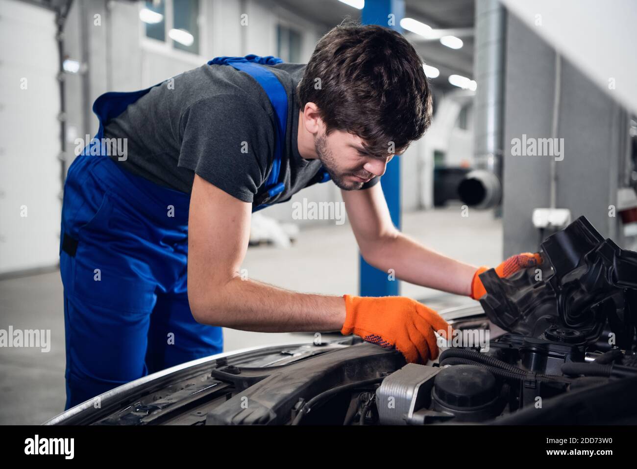 A workman is fixing a automobile engine. He is dressed in overalls and ...