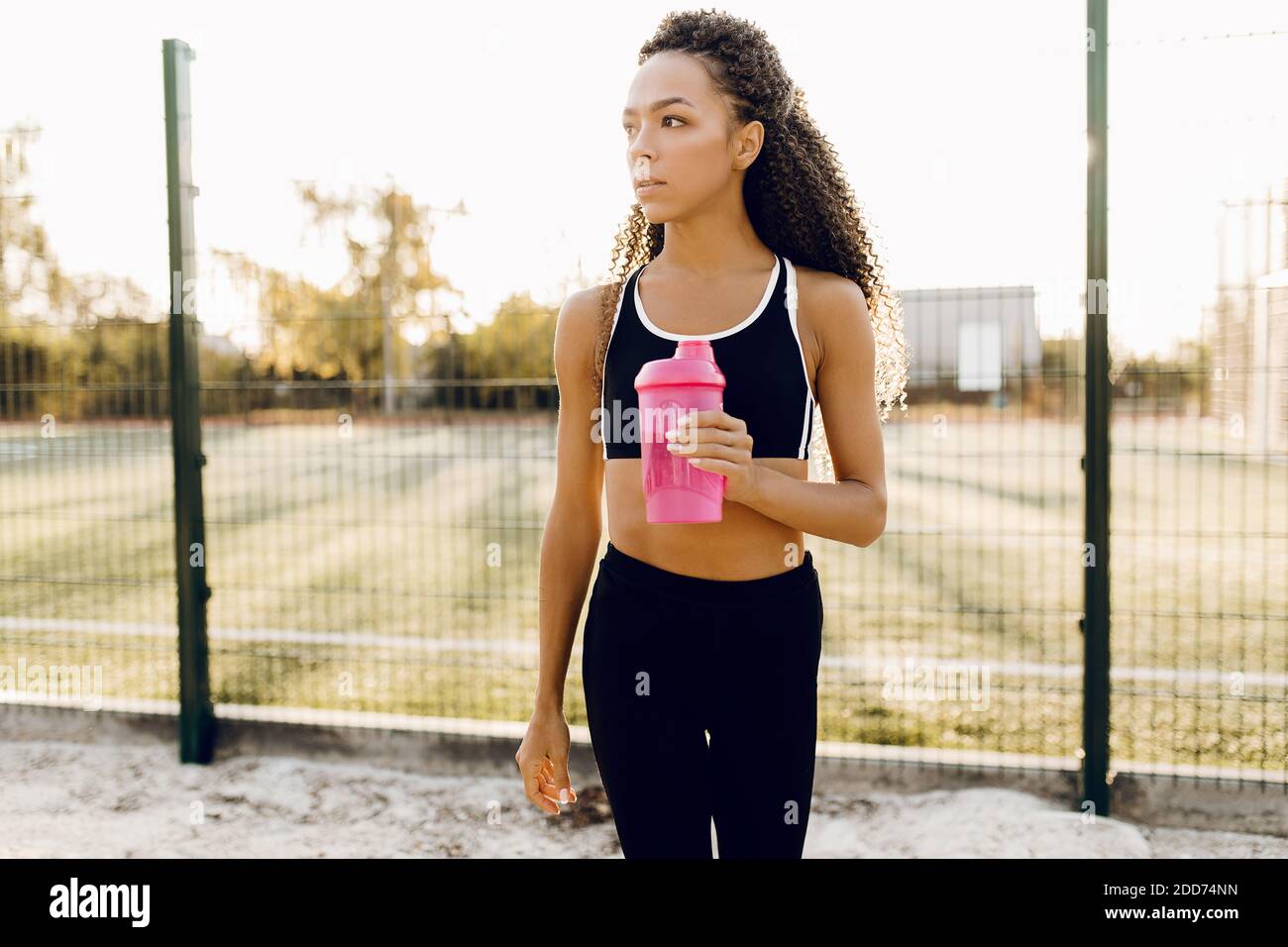 African American woman runner standing outdoors with a bottle of water ...