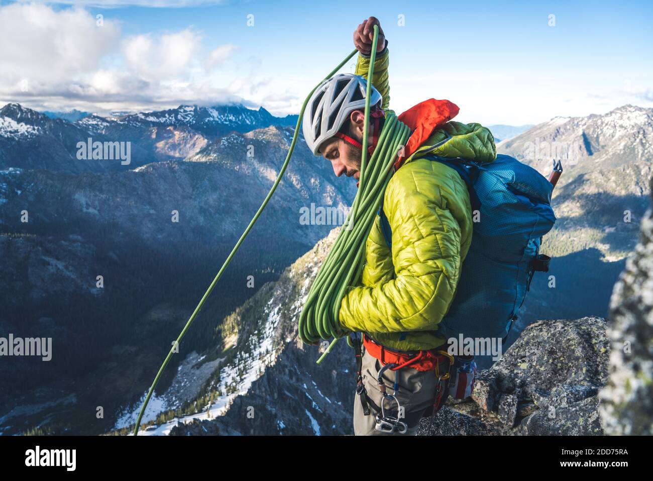 Man wearing jacket and backpack coiling rope on rock climb Stock Photo ...