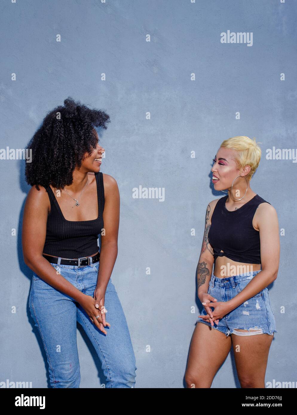 two laughing young women in identical clothes stand laughing together ...