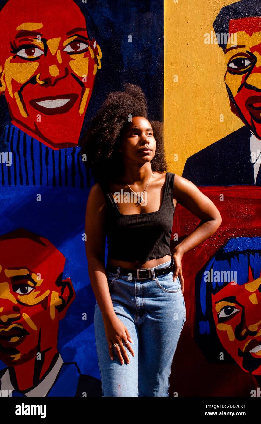 A beautiful young artist in golden light leans back against her mural ...