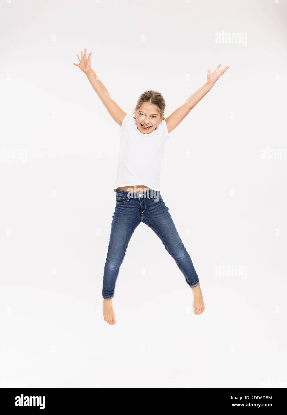 Little girl jumping with arms raised against white background in studio ...