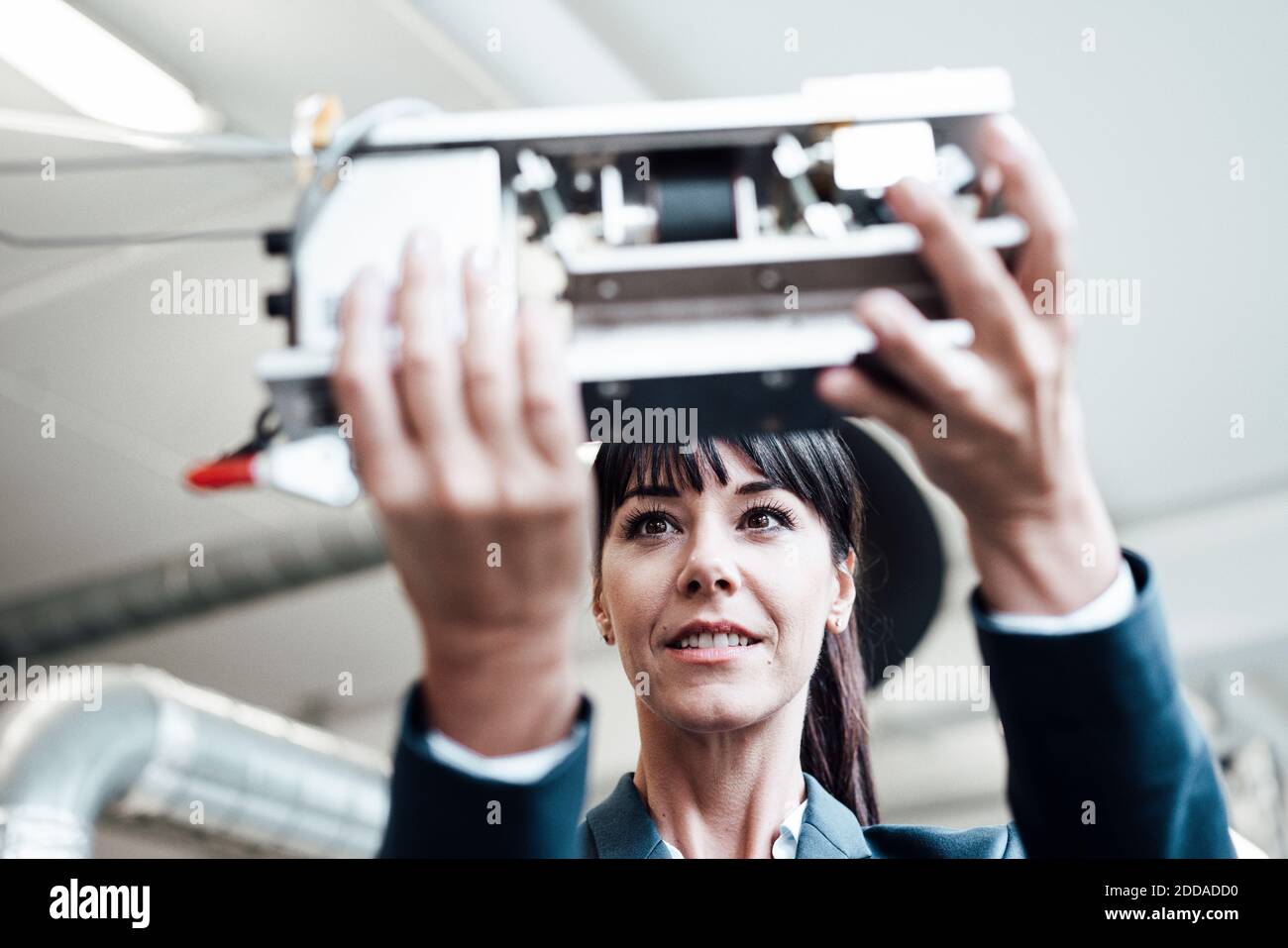 Confident businesswoman investigating while looking at machine part in ...