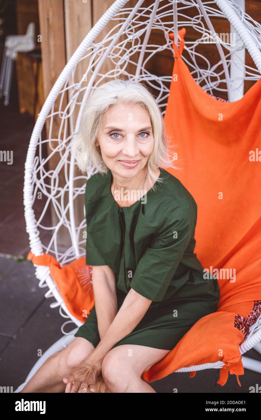 Woman smiling while sitting on hanging chair at rooftop Stock Photo - Alamy