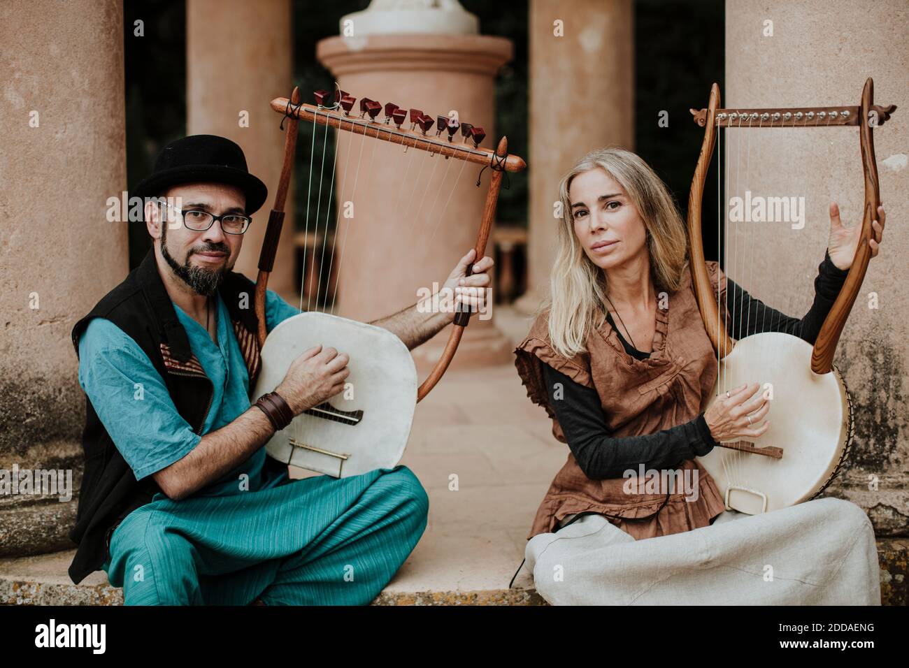 Confident female and male playing lyra musical instrument on staircase ...