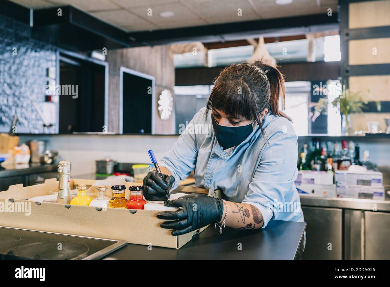 Female chef writing on take out food container in box at counter during ...