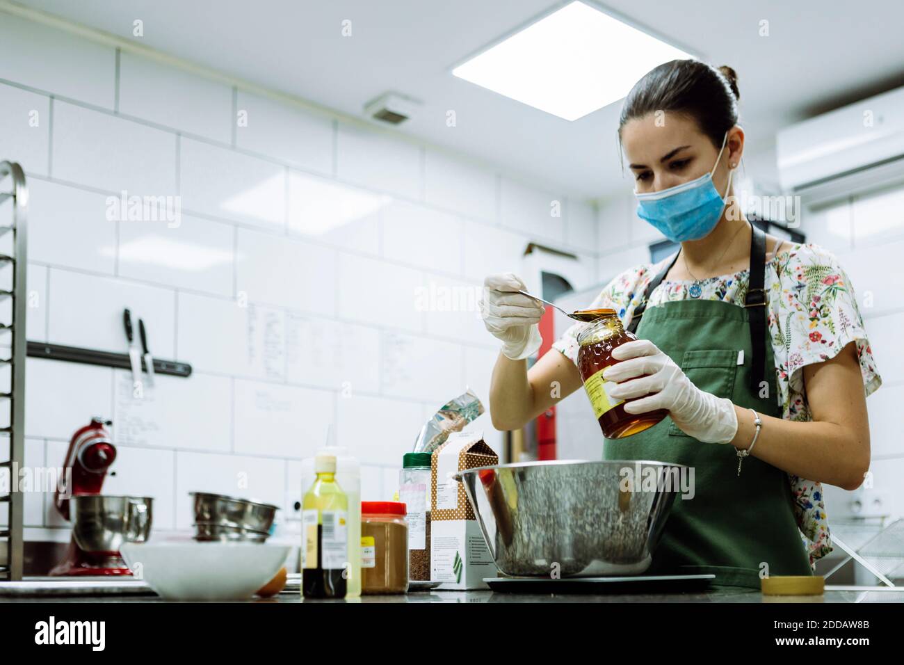 Young female baker wearing protective mask while making cookies in ...