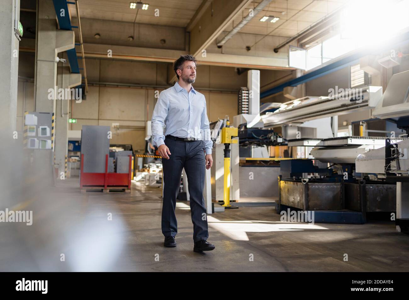 Businessman looking at manufacturing machine while walking at factory ...