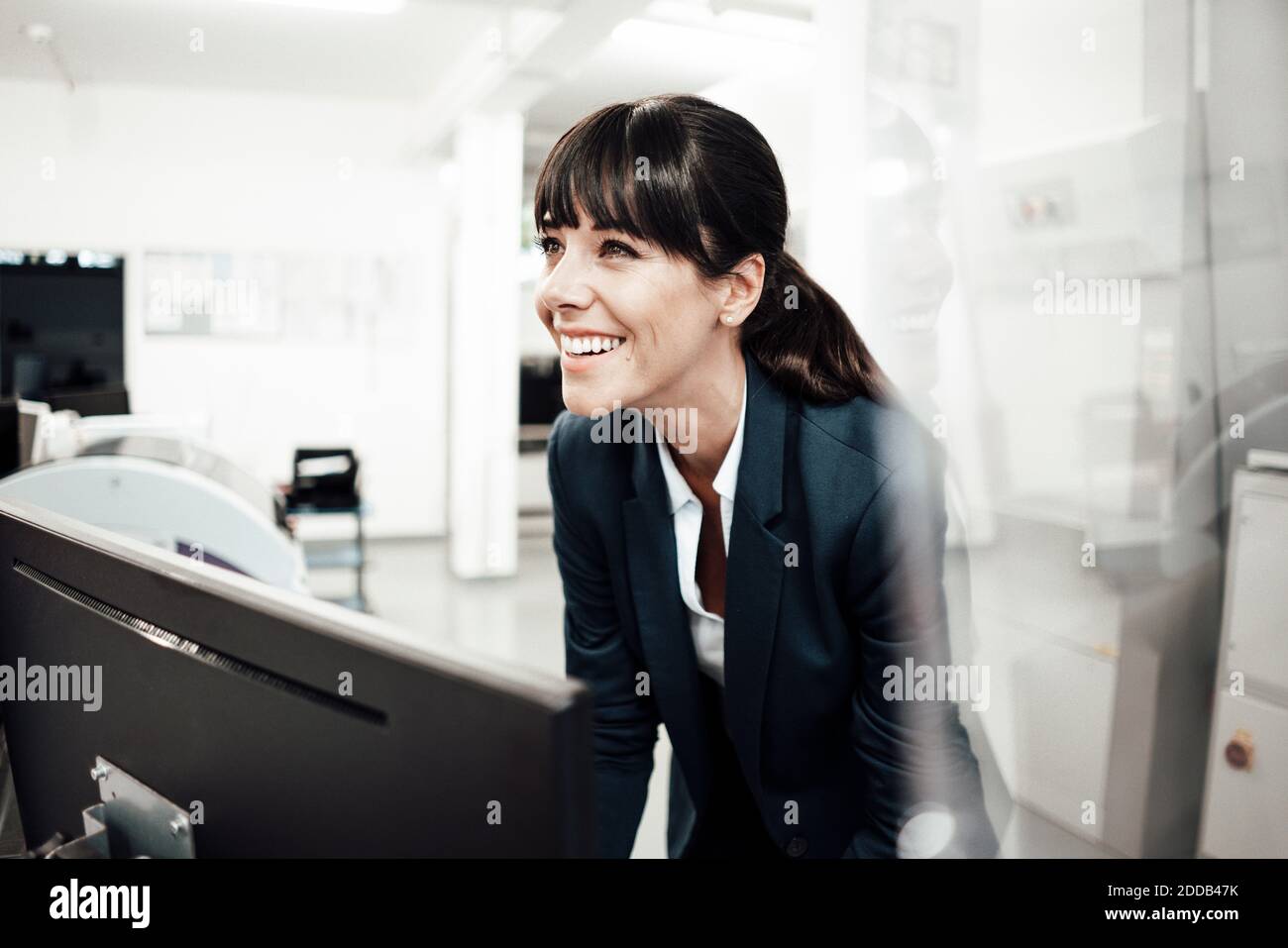 Cheerful businesswoman looking away while standing in front of computer ...