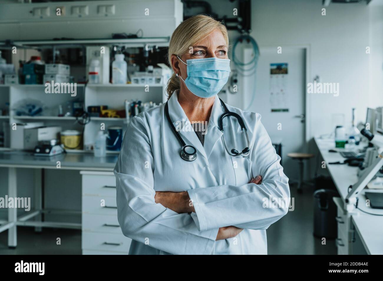 Female scientist wearing face mask standing with arms crossed at ...