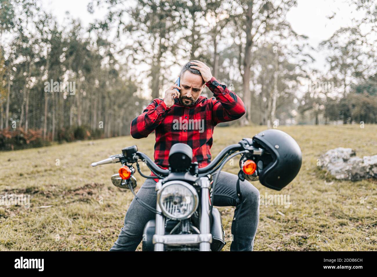 Tensed male biker talking on smart phone while sitting on motorcycle in ...