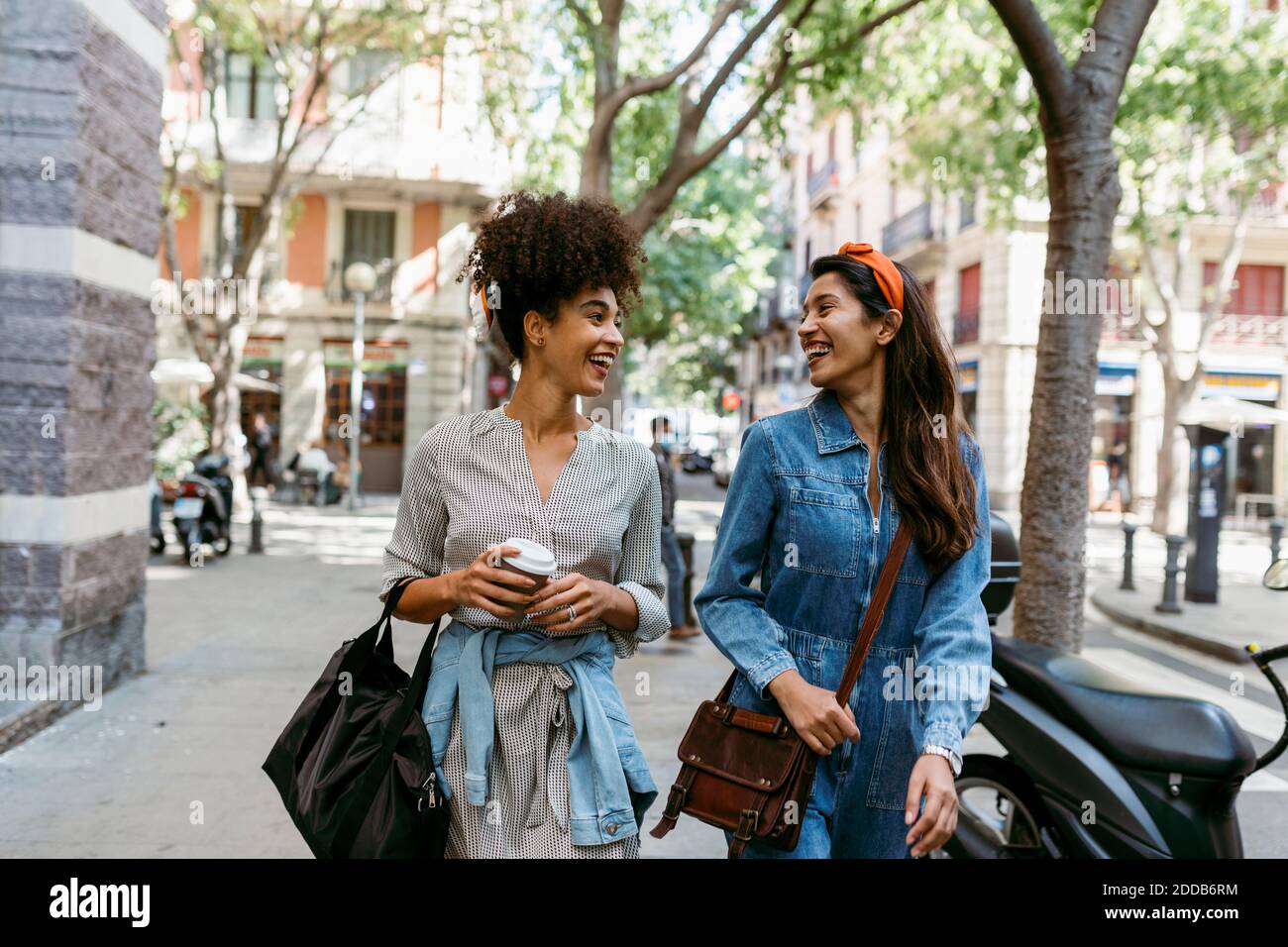 Smiling friends talking while walking at sidewalk in city Stock Photo ...