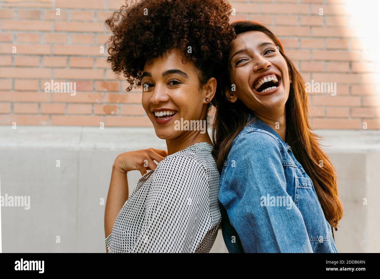 Smiling friends standing back to back against wall Stock Photo - Alamy