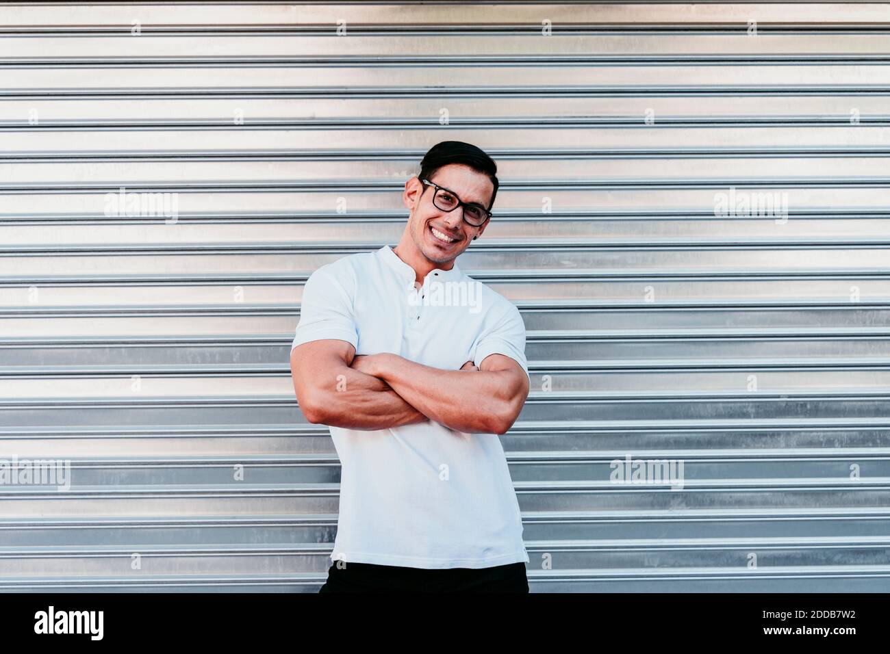 Smiling man with arms crossed standing against shutter Stock Photo - Alamy