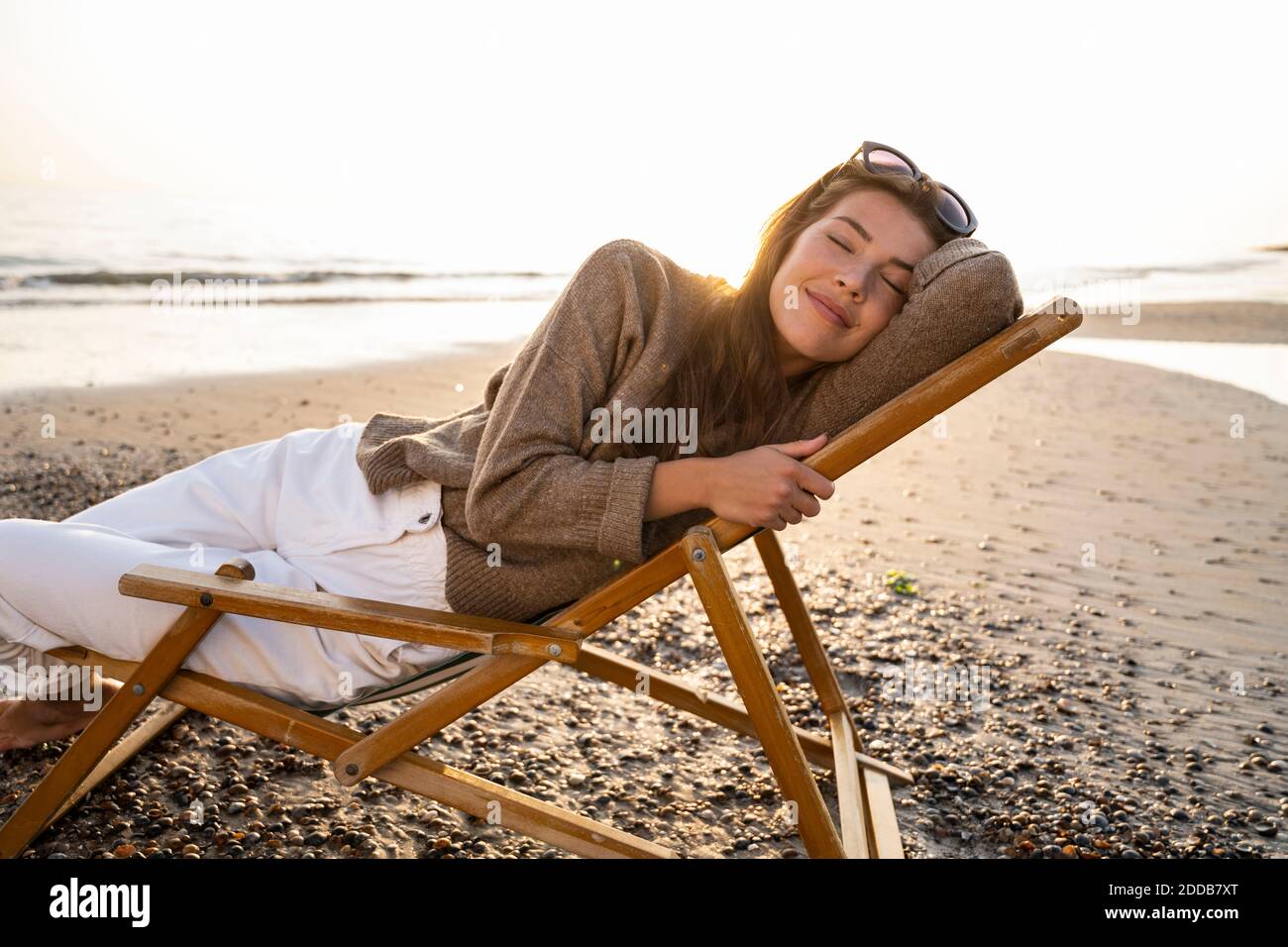 Smiling beautiful young woman reclining on folding chair while relaxing ...