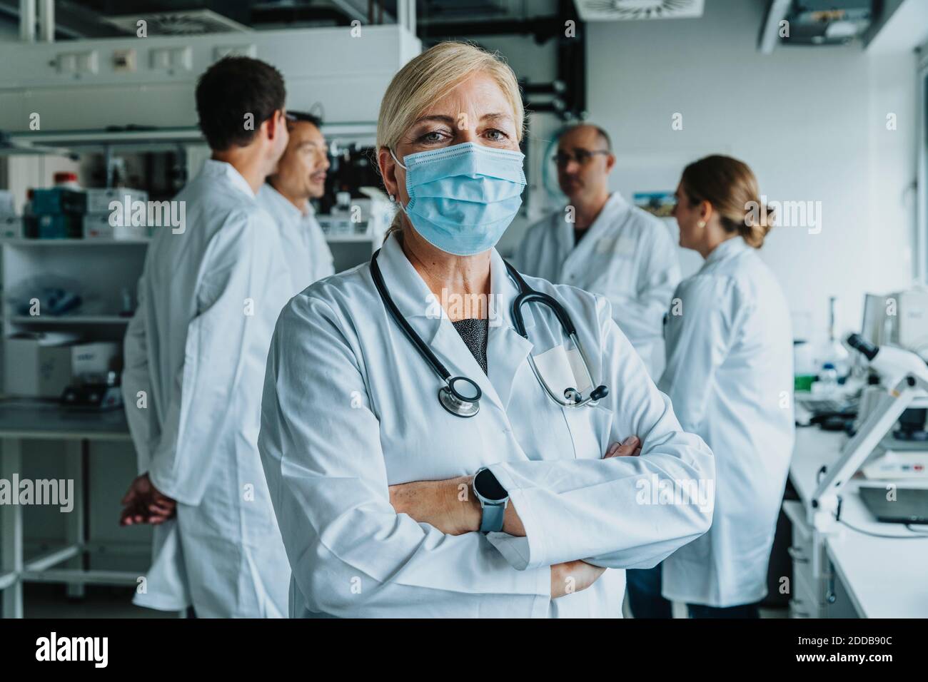 Confident scientist wearing face mask while standing with arms crossed ...