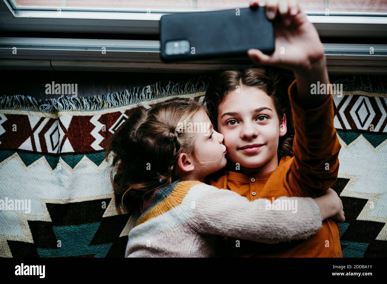 Girl Kissing Sister While Taking Selfie Through Mobile Phone At Home
