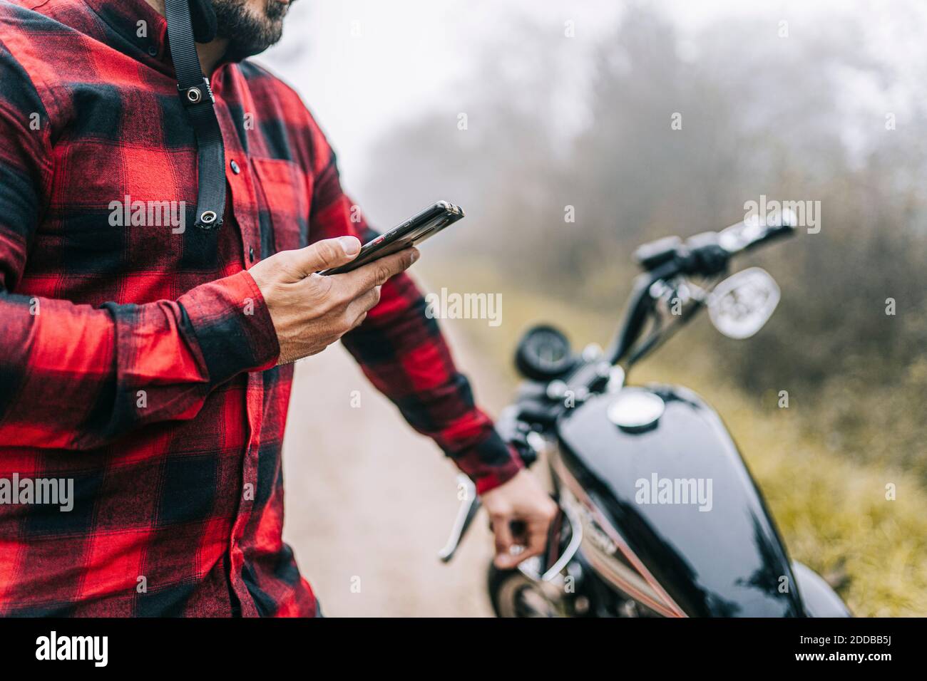 Male biker using smart phone while standing by motorcycle during road ...