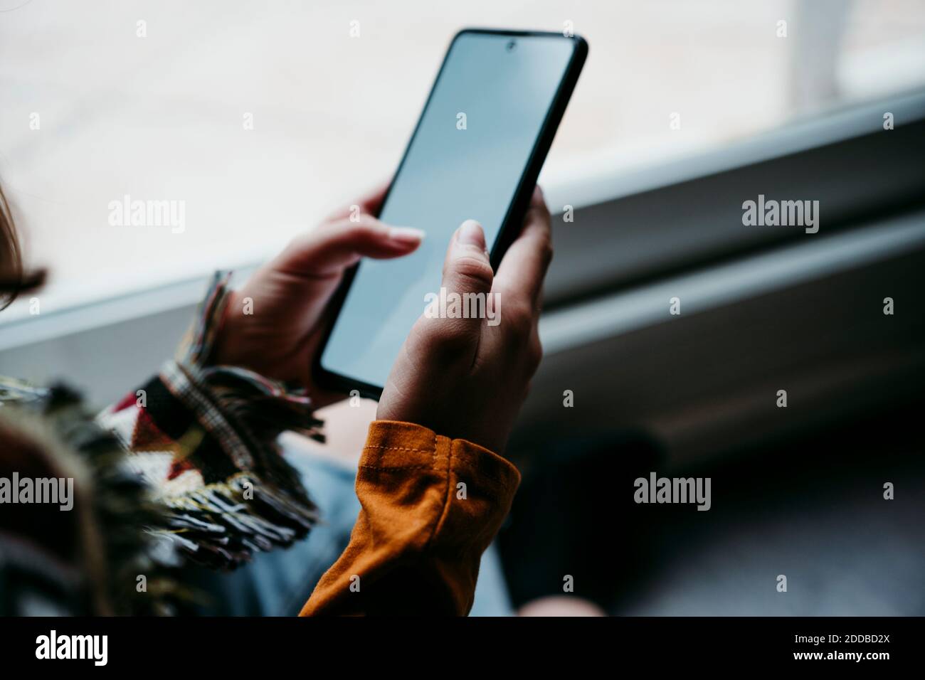 Girl using mobile phone while sitting by window at home Stock Photo - Alamy