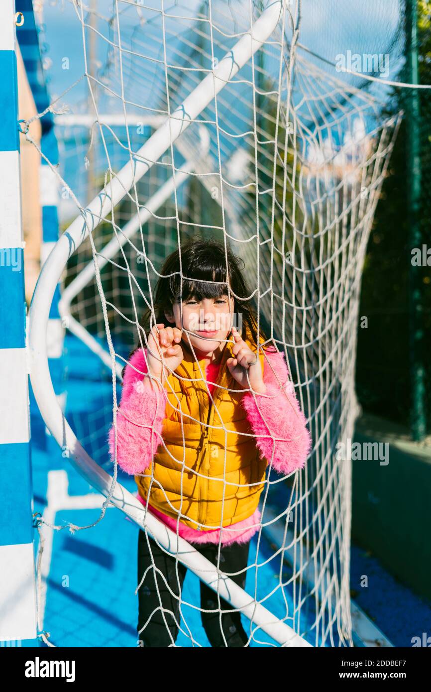 Cute girl leaning on goal post net at soccer court during sunny day ...