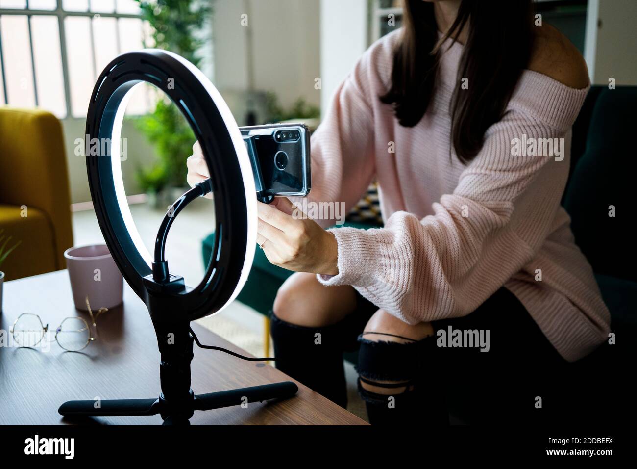Young female influencer sitting on sofa while adjusting smart phone on ...