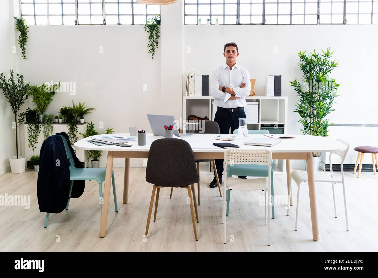 Confident male entrepreneur with arms crossed standing at desk in ...