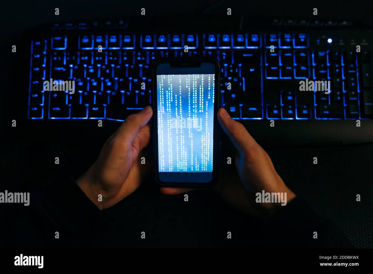 Computer hacker hand holding mobile phone against computer keyboard at ...