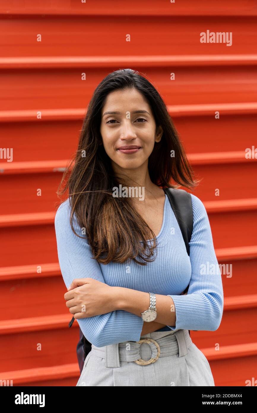 Smiling confident woman with arms crossed standing against shutter ... Smiling confident woman with arms crossed standing against shutter ...