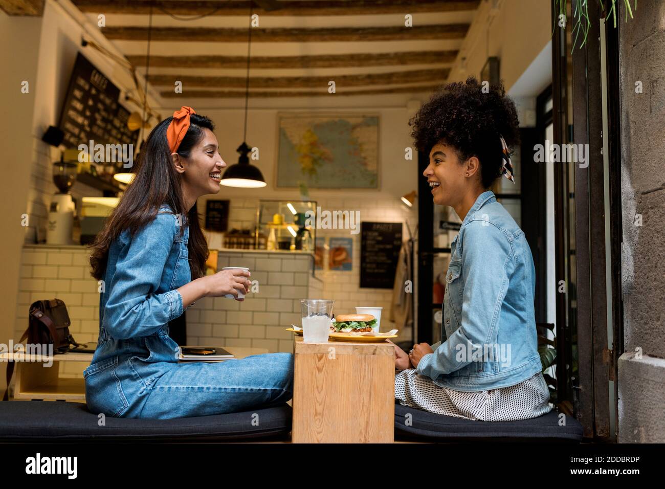 Smiling friends talking while sitting by window at cafe Stock Photo - Alamy