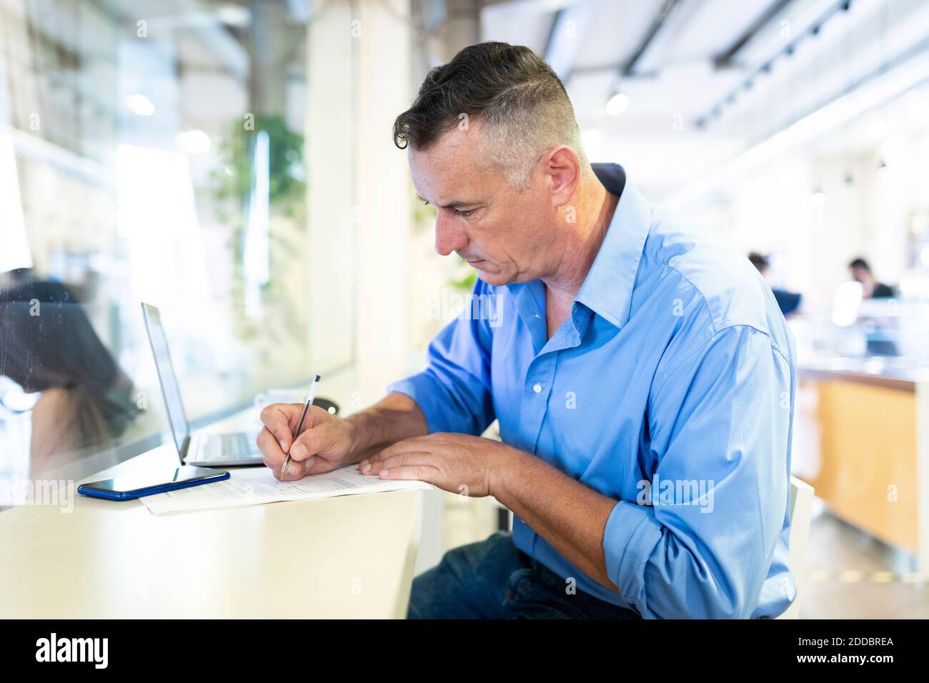 Confident male professional writing on paper while sitting with laptop ...