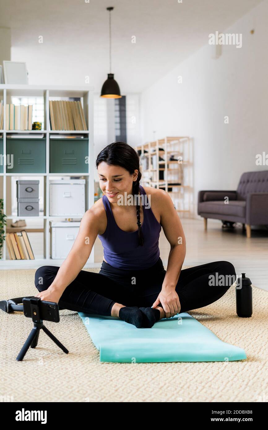 Smiling female athlete sitting in cobbler pose while video recording on ...