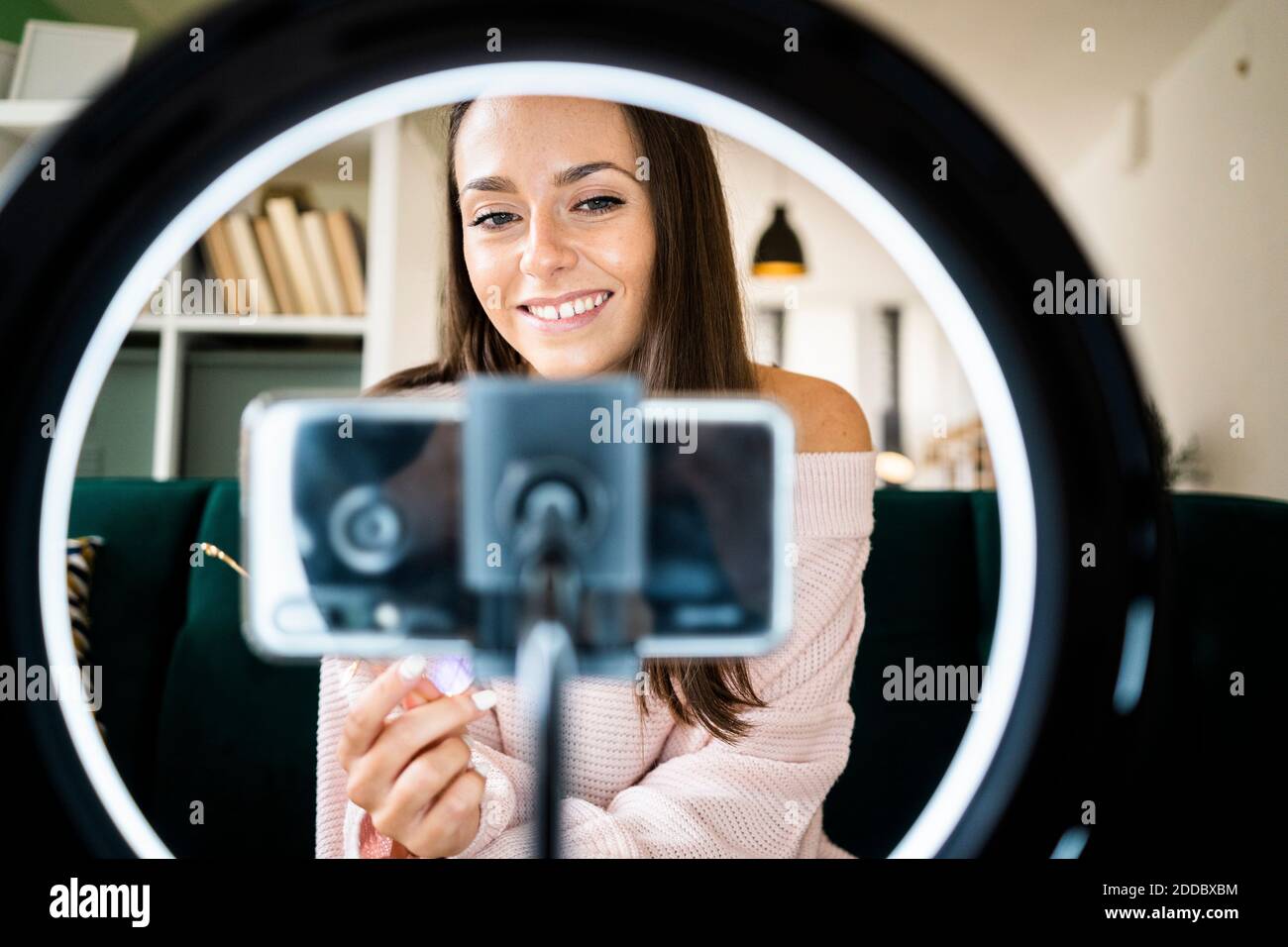 Smiling young female influencer vlogging through smart phone at home ...