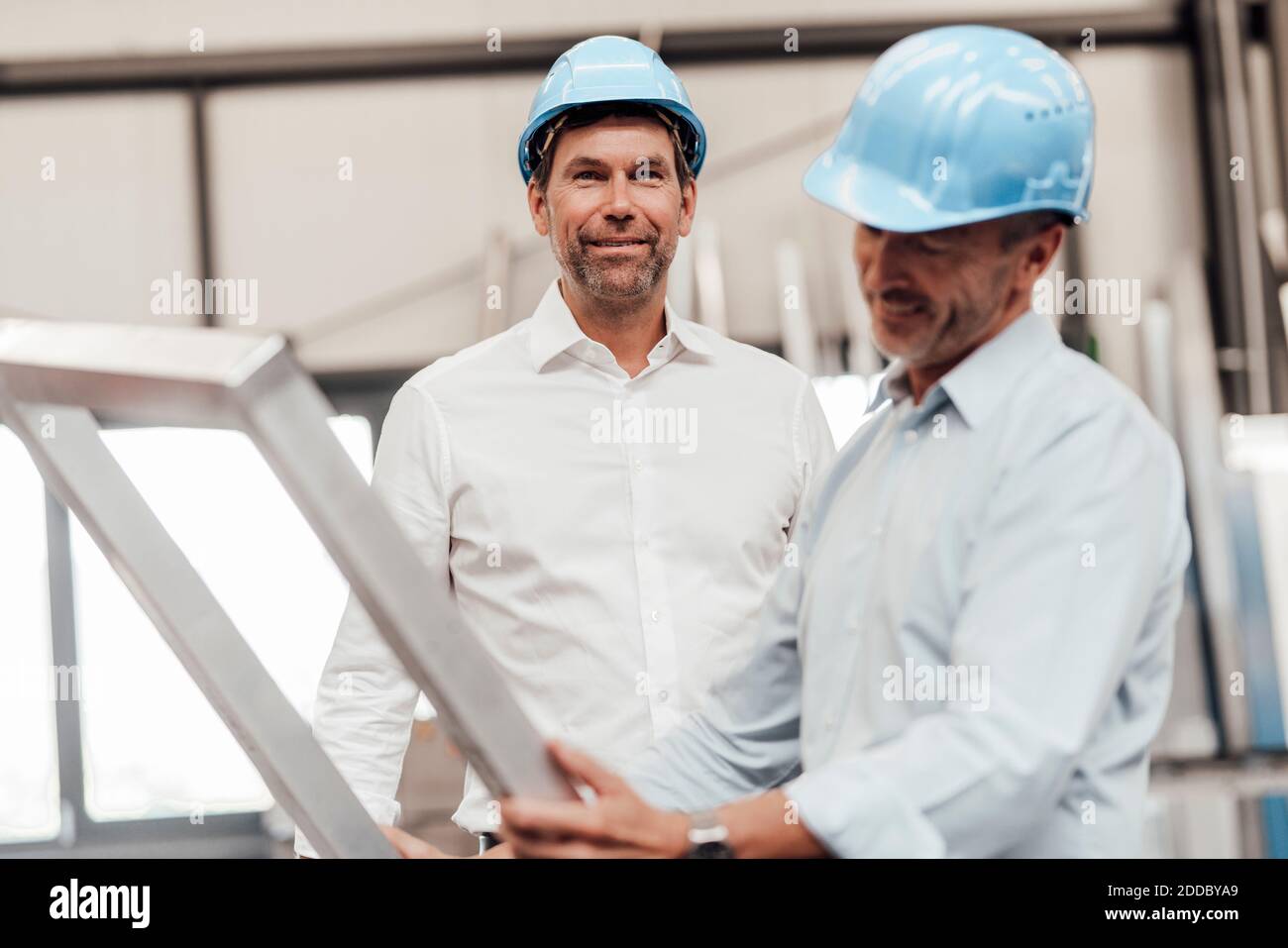 Male engineer smiling while colleague holding metallic frame in ...