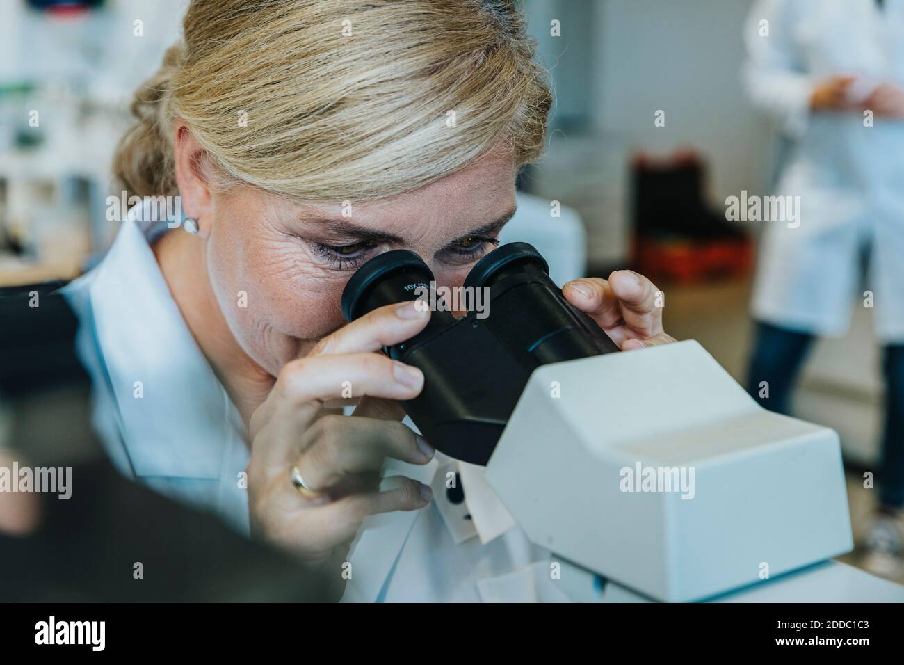 Female scientist looking through microscope while man standing in ...