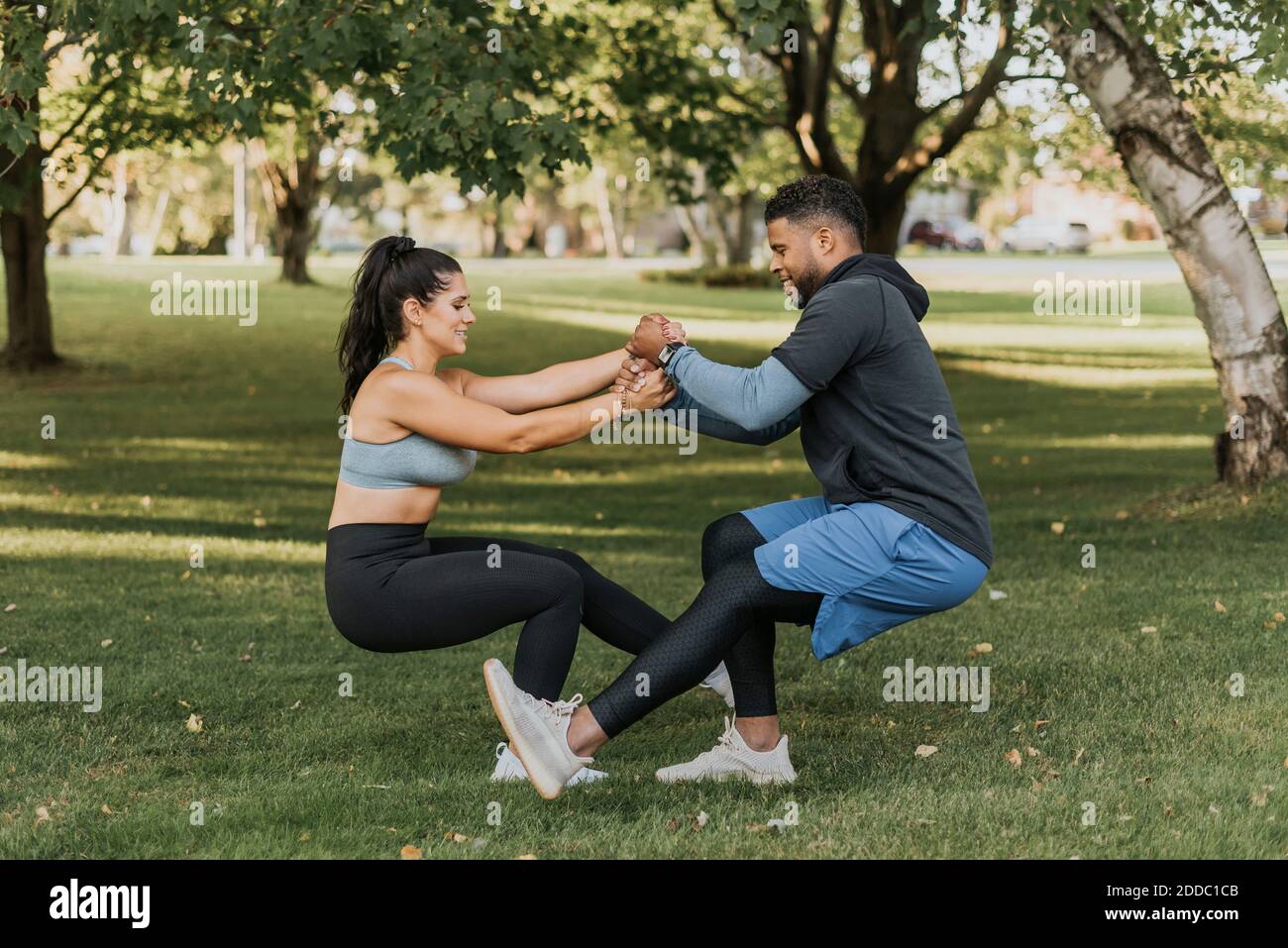 Couple holding hands while doing crouching exercise together at ...