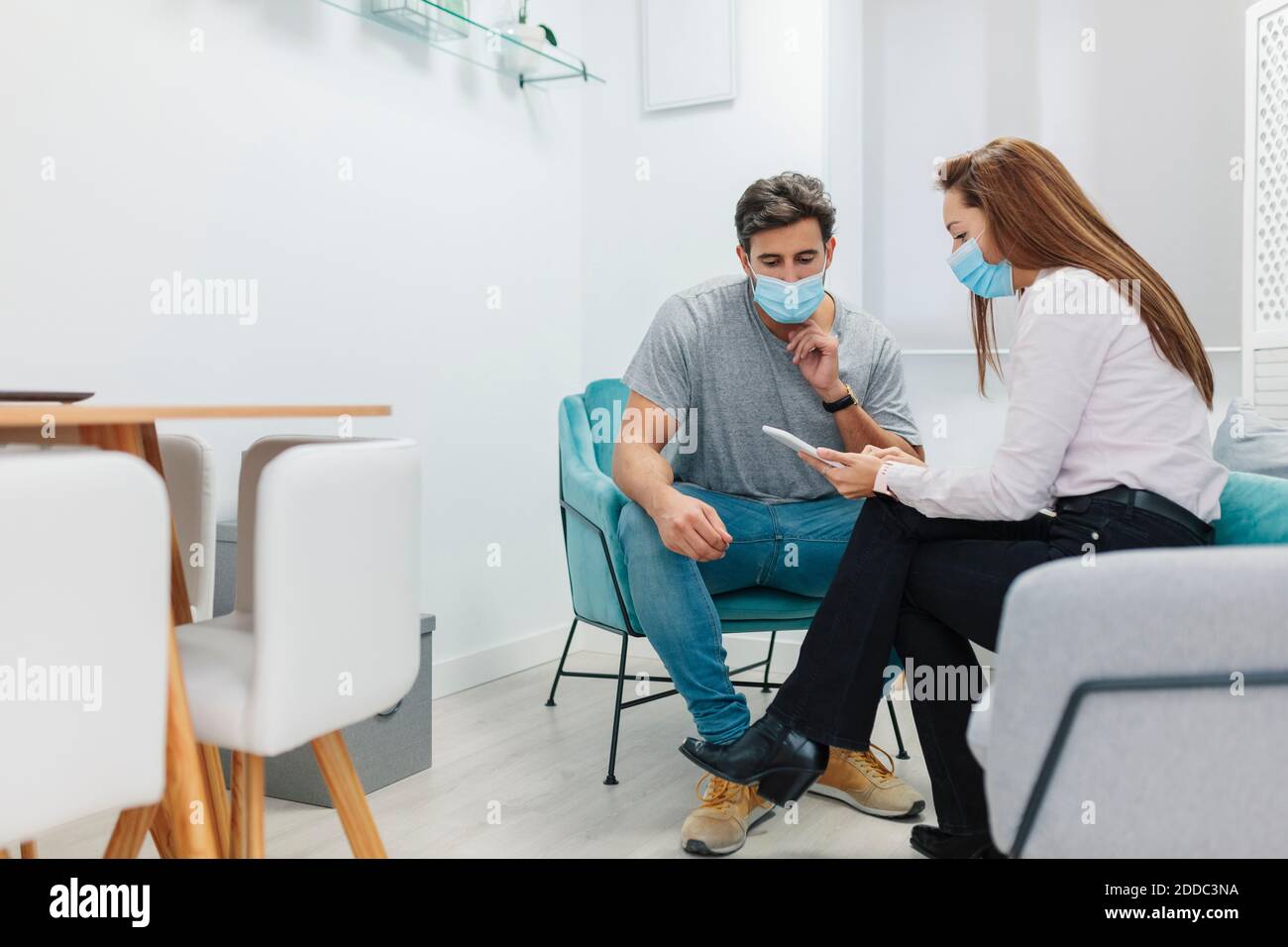 Doctor and patient wearing face mask using digital tablet while sitting ...