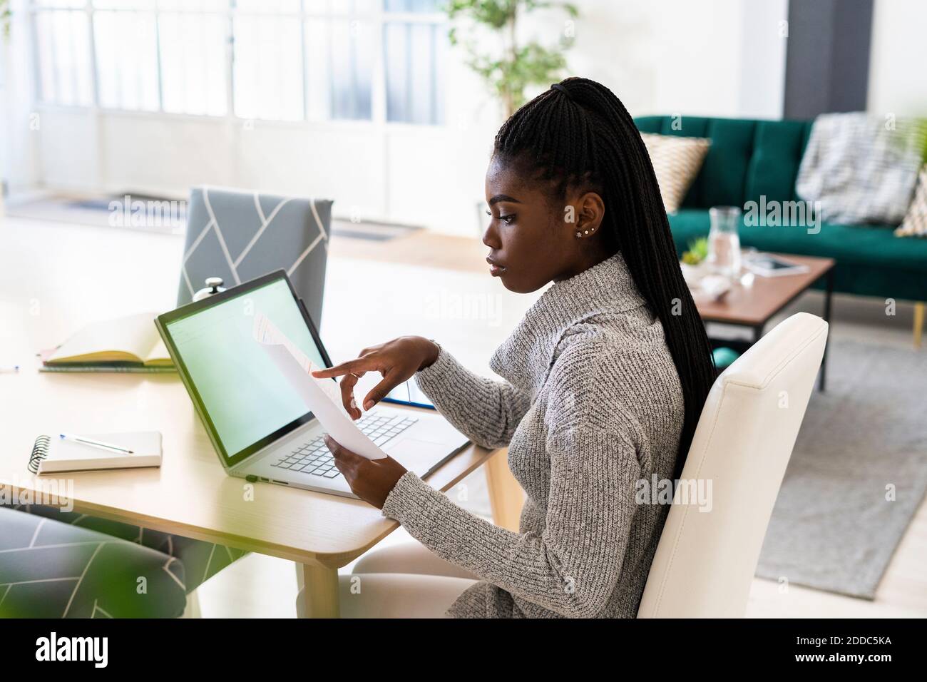 Female student reading paper while studying on laptop at home Stock ...