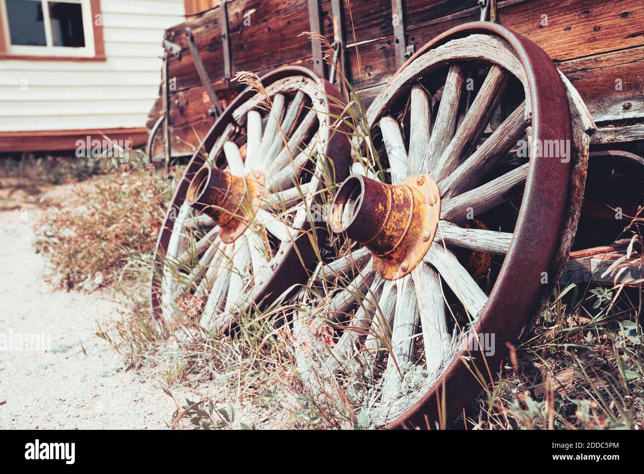 Rusty wagon wheels against a wooden cart, with grass. Useful for rustic ...